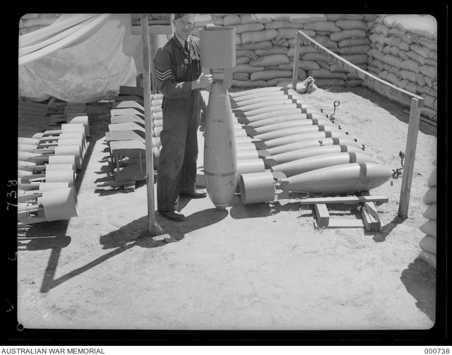 Laverton - A RAAF Sergeant stands and supports a 500 lb bomb. Others ...