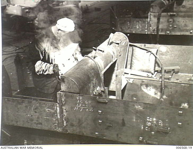 THIS WELDER, AT WORK ON THE NOSE OF THE HULL, WEARS A WHITE CAP TO ...