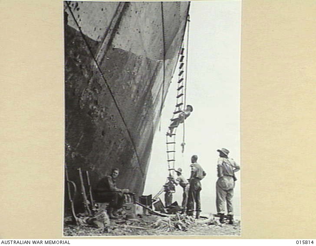 NEW GUINEA. FALL OF LAE. SOLDIERS BESIDE THE HULL OF THE WRECKED ...