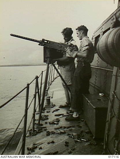 Two men man a .50 Browning machine gun, spent shells lie on the deck ...
