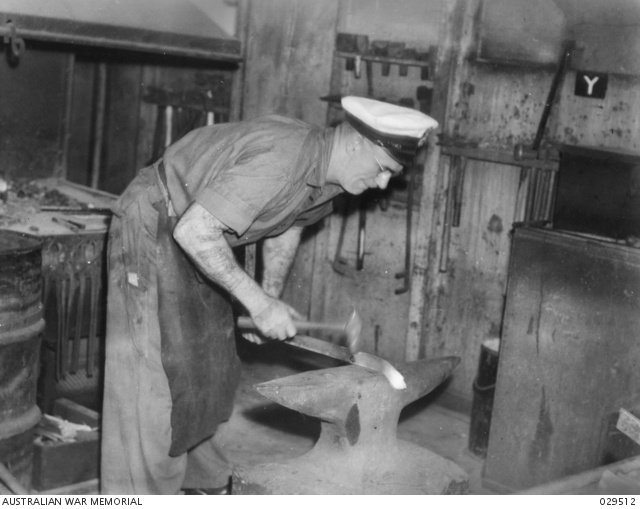HMAS AUSTRALIA, AT SEA. 1943-02. BLACKSMITH J.C. MACKIE WORKING IN THE ...