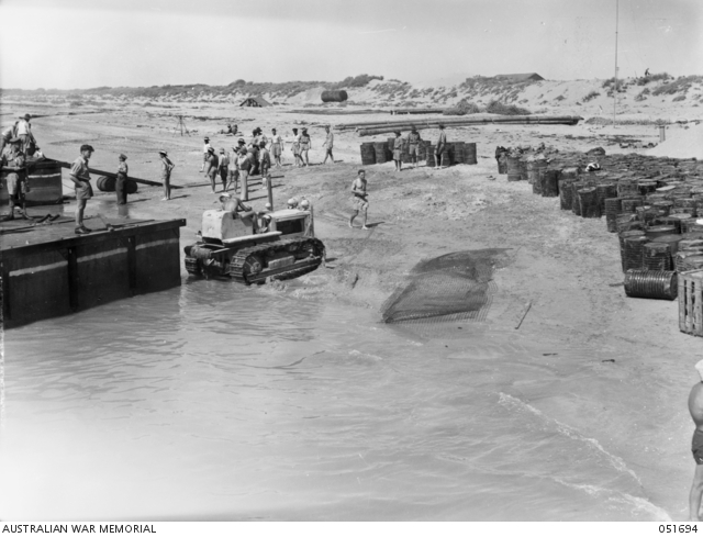 POTSHOT, WA. 1943-04-28. UNLOADING DRUMS OF BITUMEN FROM BARGES, FOR ...
