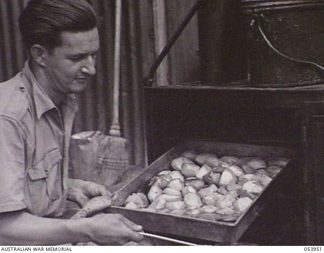 YUNGABURRA, QLD. 1943-07-08. COOKING ROAST POTATOES IN AN OPEN OVEN AT ...