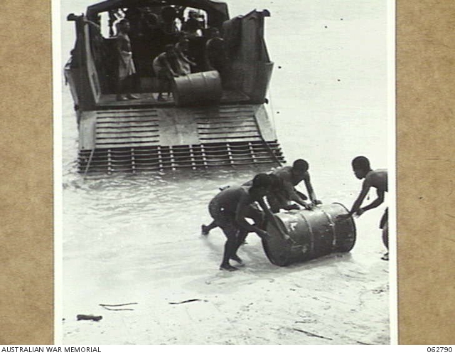 SIALUM BEACH, NEW GUINEA. 1944-01-08. NATIVES UNLOADING 44 GALLON DRUMS ...