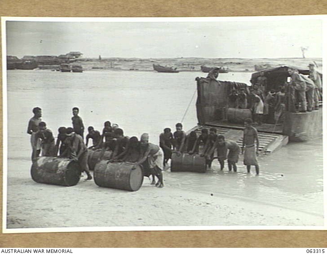 SIALUM BEACH, NEW GUINEA. 1944-01-07. NATIVES UNLOADING 44 GALLON DRUMS ...