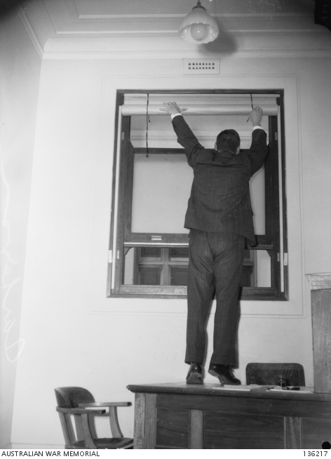 CANBERRA, ACT. 1942-03. A MEMBER OF THE STAFF FITTING BLACKOUT CURTAINS ...