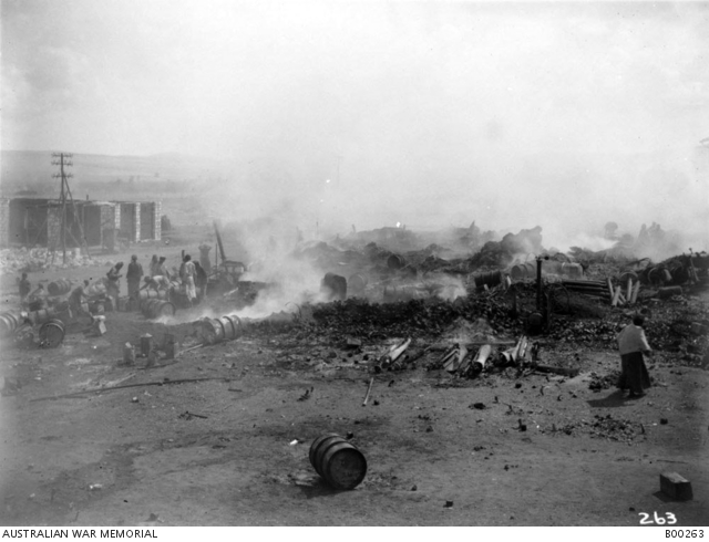 A railway dump on fire. At left some local people are salvaging drums ...