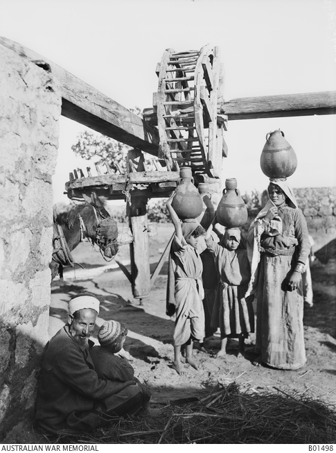 Native water carriers standing by an old water wheel in the village of ...