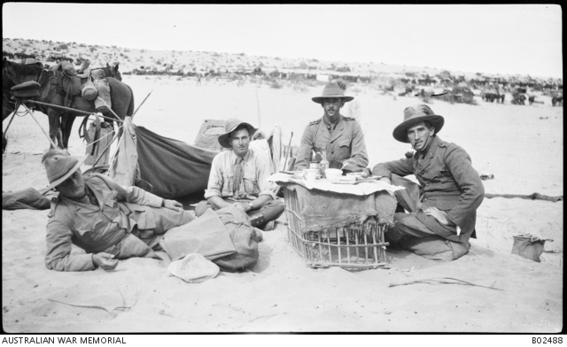 Lunch in the desert. Sitting on the ground with a crate for a table are ...