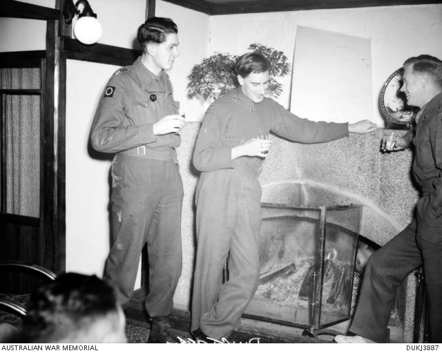Three unidentified servicemen enjoy a drink by a fireplace in a lounge ...