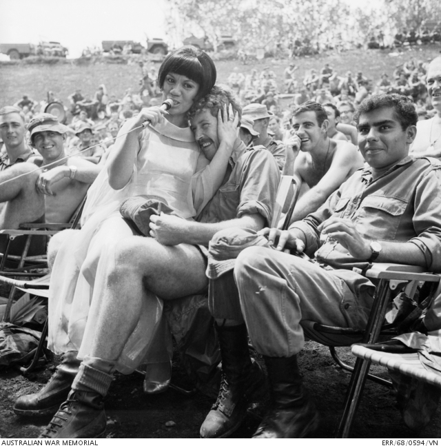 Entertainer Joy Yates, sitting in the lap of one of the troops of the ...