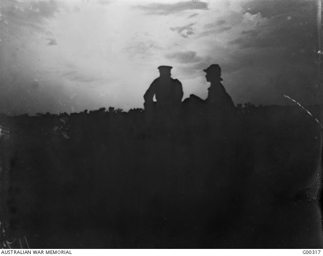 Two soldiers silhouetted against the night sky lit up by the fire of ...