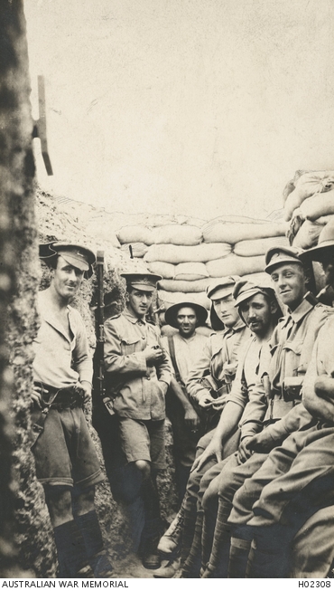A group of soldiers standing below a parapet with sandbags after being ...