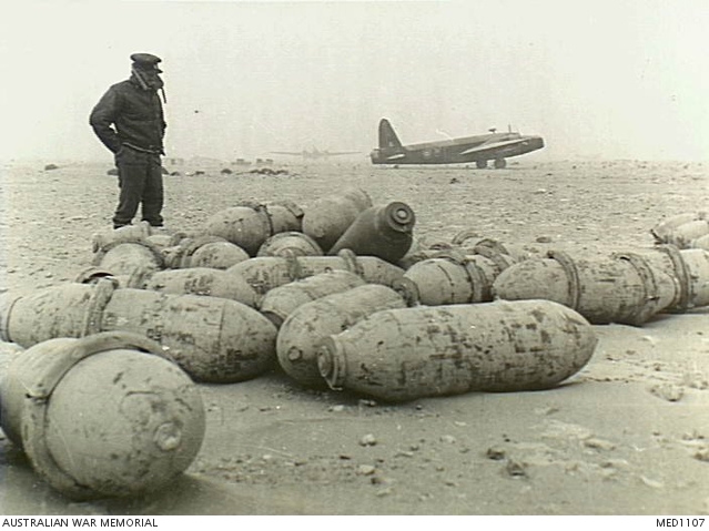 Bombs as big as a man lie on the sand at an airfield. They are ready to ...