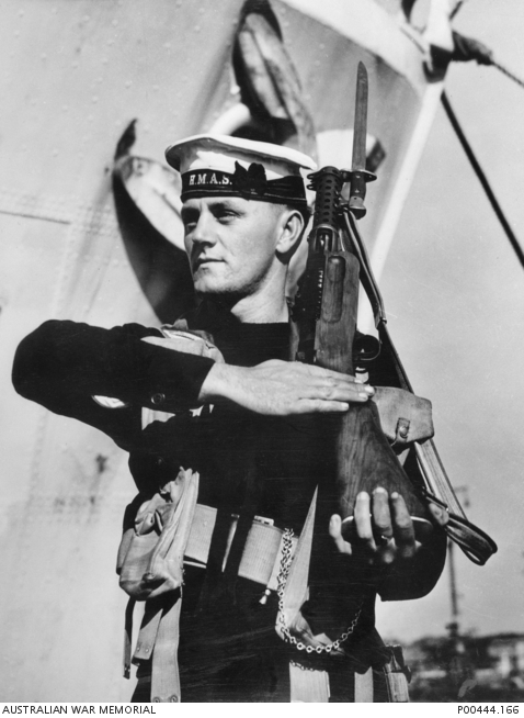 A RATING OF THE RAN SALUTING WHILE ARMED WITH A LANCHESTER SUBMACHINE ...