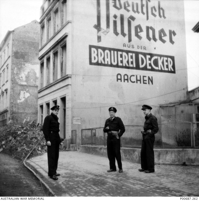 JOHN TOOHEY, JACK FLOWER AND JACK YOCOM BESIDE A BUILDING ADVERTSING ...