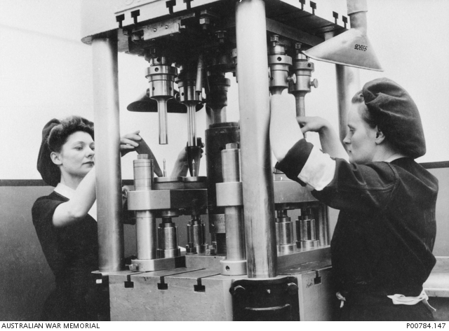 c. 1944. Two women charge a machine press for filling of explosive ...