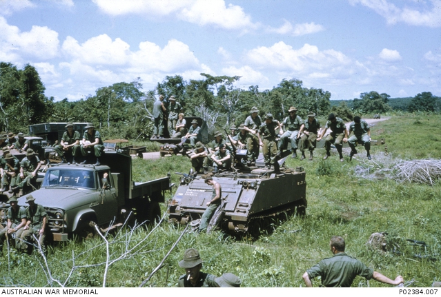 A large crowd of Australian soldiers sits on army trucks and a recovery ...