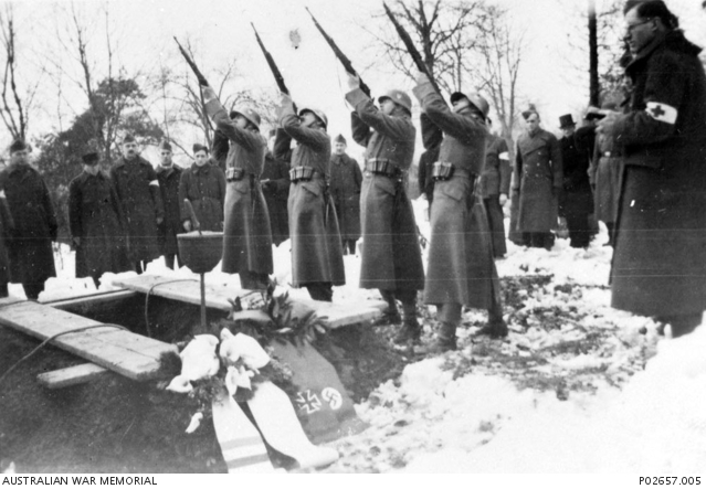 A German firing party with their rifles raised next to a grave ...
