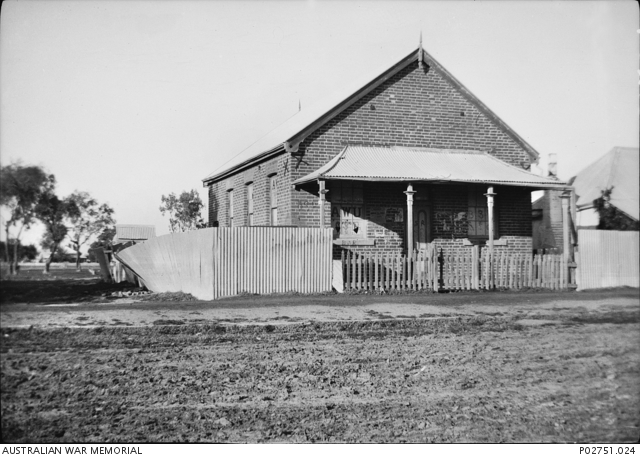 A disused brick building with wooden fence seen from the front. Note ...