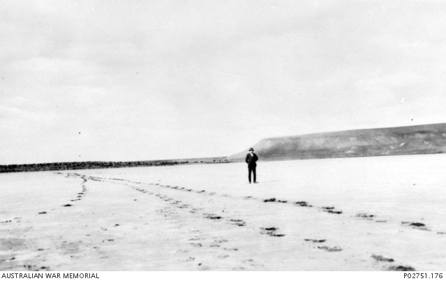 A man standing on a flat, desolate plain with a hill on the right of ...