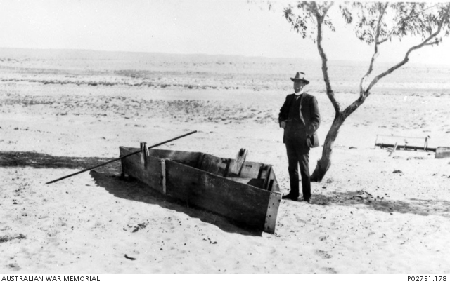 A man standing in front of a small gum tree on a flat, desolate plain ...