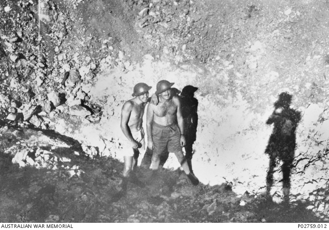 Two radio personnel standing in a large bomb crater in the main street ...