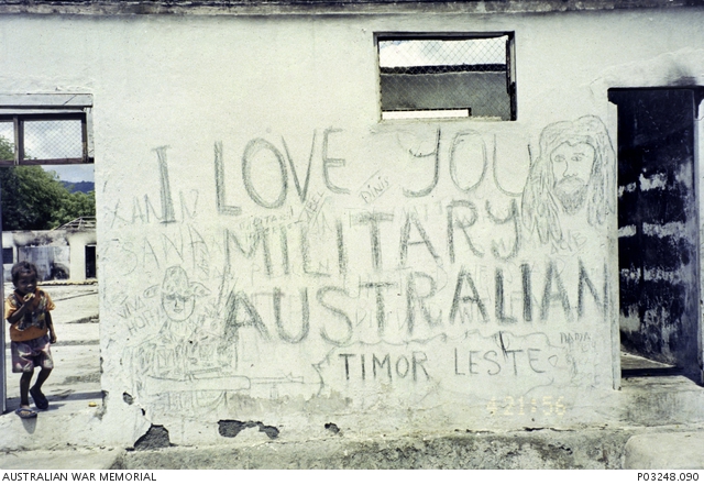 Graffiti on the wall of a destroyed building in the Suai market place ...