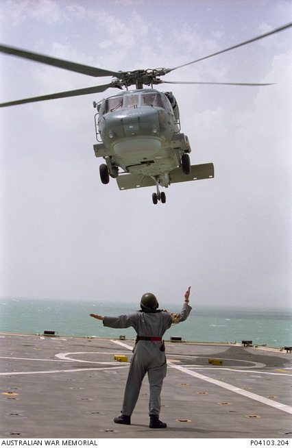A crew member on board HMAS Kanimbla signals to the pilot of an S-70B-2 ...