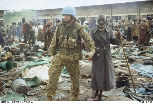 An Australian soldier leading an elderly blind man through the debris ...