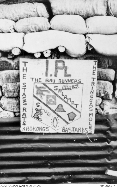 Attached to a sand bagged wall, hangs a sign, handmade by 1st Platoon ...