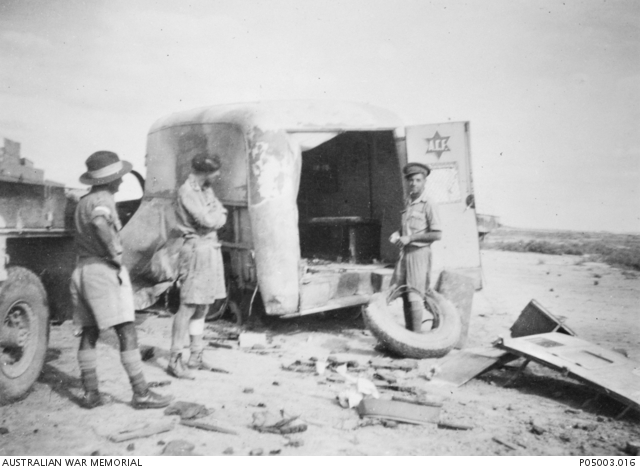 Three unidentified servicemen survey the wreckage of a 1939 Ford panel ...