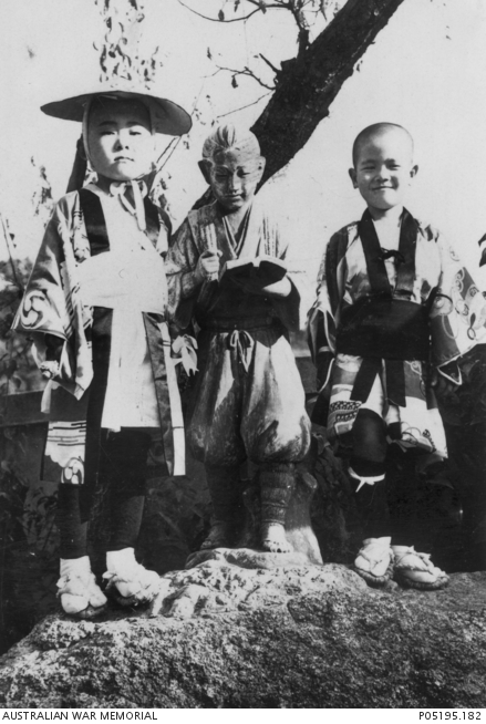 Portrait of two young Japanese boys standing either side of a stone ...