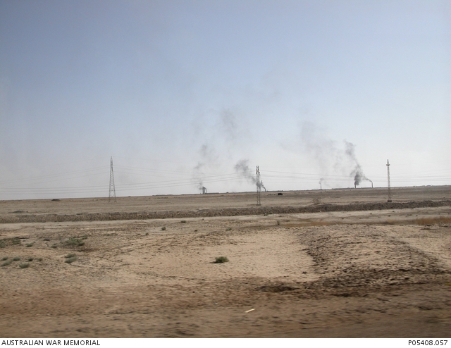 Smoke rising from oil refineries in the distance in an oil field along ...