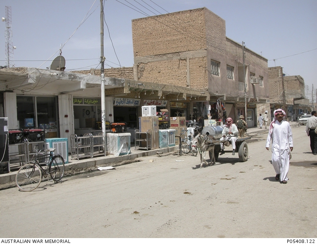An Iraqi man driving a cart, pulled by a donkey, down a street in Ar ...