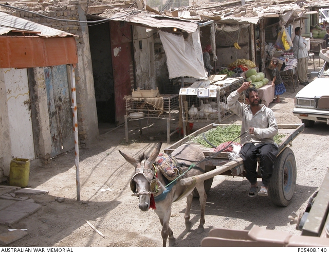 A man driving a small, flat, wooden cart pulled by a donkey through the ...