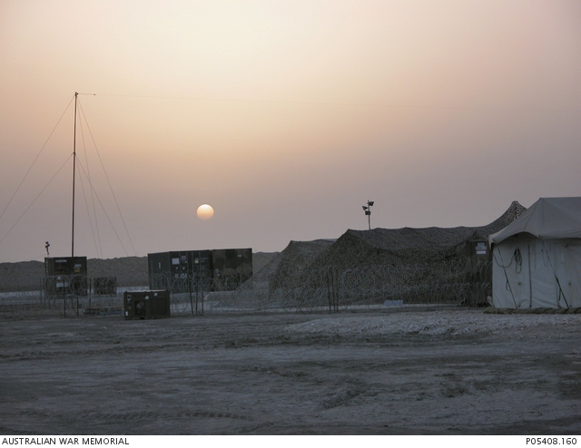 The sun setting over storage containers, tents and barbed wire in Camp ...