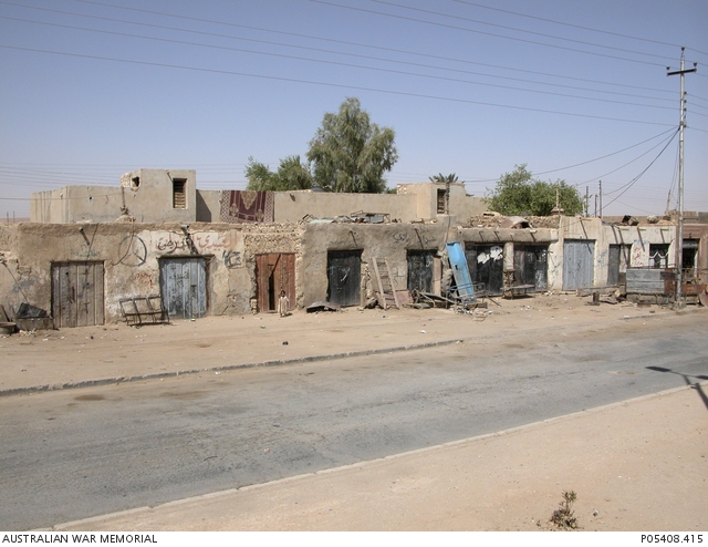 A young Iraqi child standing in front of a row of damaged and derelict ...