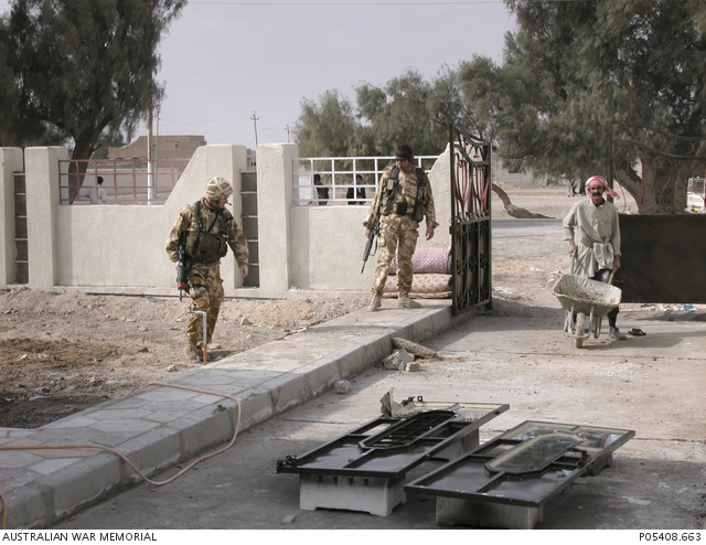 A local Iraqi building contractor pushing a wheelbarrow past two ...