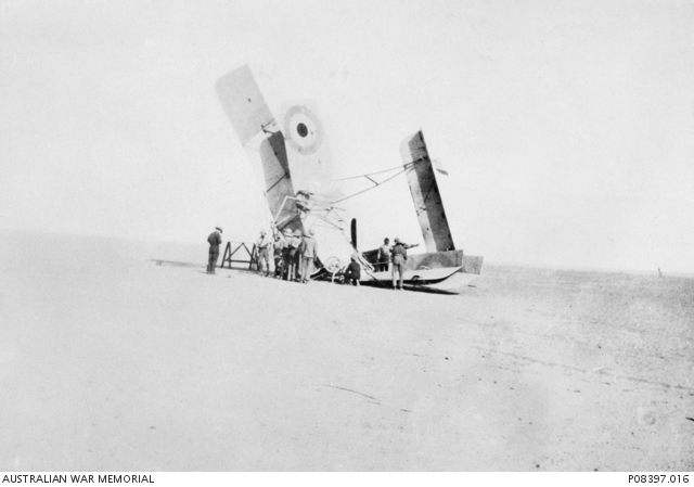 Soldiers stand around the wreckage of a crashed biplane. This image is ...