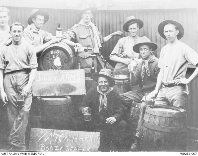 Group portrait of servicemen at a make shift bar. The signs read ...