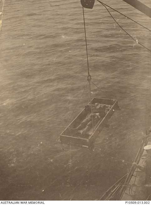 Oblique view of a wounded man in a cradle being hoisted aboard a ...