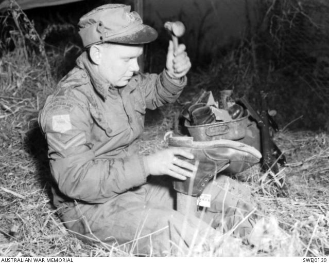 A camouflaged tent serves as a temporary cobbler's shop for 41308 Corporal (Cpl) Stanley Vincent ...